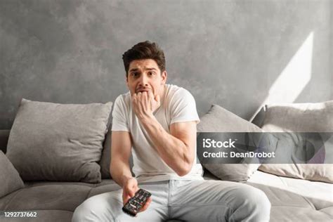 회색 아파트의 소파에 앉아있는 동안 두려움에 주먹을 물고 손에 Tv를위한 원격 제어를 들고 무서운 남자의 사진 30 39세에 대한 스톡 사진 및 기타 이미지 Istock