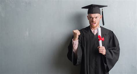 회색 그런 지 이상 젊은 빨강 머리 남자 벽 화가 학위를 들고 대학원 유니폼 입고 및 미친과 제기 손으로 소리 분노와 좌절