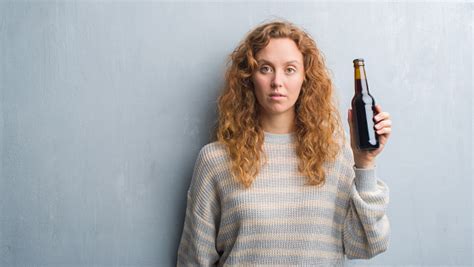 스마트 얼굴 심각한 생각에 자신감이 표정으로 맥주 병을 들고 회색 그런 지 벽에 빨강 머리 젊은 여자 감정에 대한 스톡 사진 및