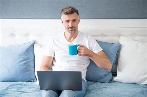 Premium Photo Mature Man Smile Using Computer In Bed With Coffee