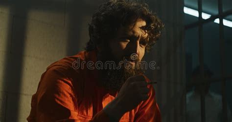 Upset Prisoner Sits On Bed In Prison Cell Smokes Cigarette Stock Image