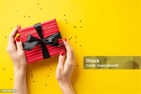 블랙 프라이데이 개념 고립된 노란색 배경에 검은 색종이 위에 리본 리본 활이 있는 빨간 선물 상자를 들고 있는 여자의 손의 1