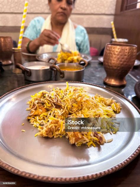 금속판에 치킨 비리야니 사프란 필라우 쌀을 얹은 테이블 세트의 클로즈업 이미지 파란색 살와르 카메즈 전통 의상을 입은 인도 여성 흰색 두파타 배경 전경에 초점 근거리 초점에