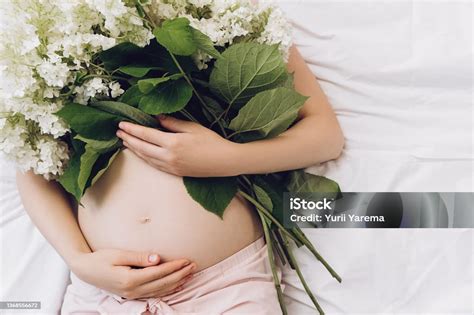 아름다운 신선한 여름 꽃을 들고 편안한 침대에 누워 부드럽게 배를 만지는 젊은 임신 한 여성의 손을 닫습니다 미래의 어머니의 기대 공간을 복사합니다 개념 모성 20 24세에