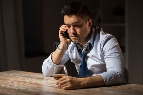 酒精中毒、酒精成瘾和人们的观念——男性酗酒者晚上喝白兰地并打电话给智能手机。高清摄影大图 千库网