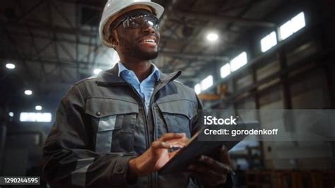 안전 유니폼과 하드 햇을 착용한 전문 중공업 엔지니어 작업자는 태블릿 컴퓨터를 사용합니다 금속 건설 제조에서 걷는 아프리카 계