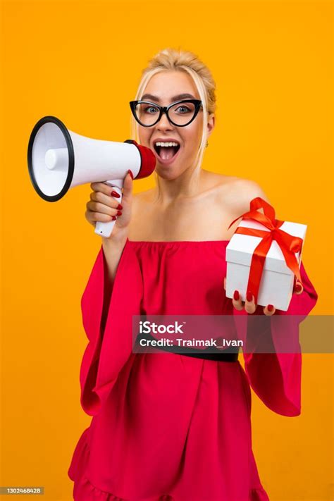 빨간 드레스를 입은 금발 소녀가 메가폰을 들고 있는 선물과 노란 배경에 손에 선물 상자를 들고 있는 것에 대해 이야기합니다 18 19세에 대한 스톡 사진 및 기타 이미지