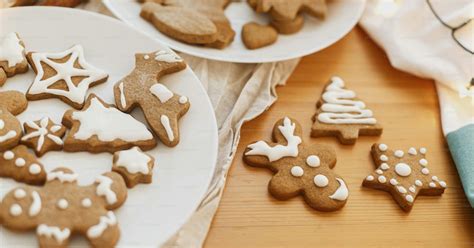 축제 조명이 있는 나무 테이블에 흰색 접시에 장식된 진저브레드 쿠키 크리스마스 트리 별과 순록 쿠키를 설탕 프로스팅으로 장식했습니다 크리스마스 휴일 전통과 출현 사진