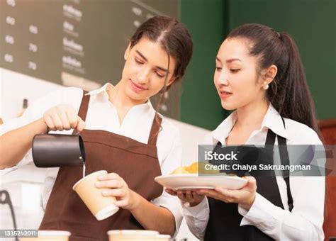 카페 커피숍에서 메뉴를 배경으로 한 고객을 위해 테이크아웃 핫 커피와 빵을 준비하는 백인과 아시아 바리스타 여성의 반몸 각도 2