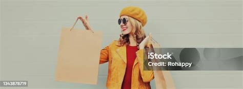 노란 재킷을 입은 쇼핑백과 함께 아름다운 행복한 미소 짓는 젊은 여성의 가을 초상화 회색 배경에 베레모 25 29세에 대한 스톡 사진 및 기타 이미지 Istock