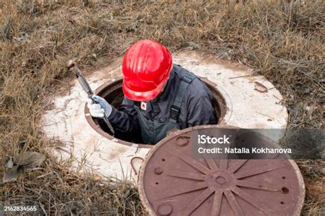헬멧을 쓴 작업자가 조정 가능한 렌치를 사용하여 우물에 앉아 있습니다 급수 장치의 유지 보수 및 수리 50 54세에 대한 스톡 사진 및 기타 이미지 Istock