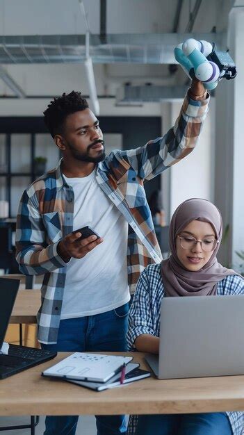 black male engineer raises robotic arm with controller while female