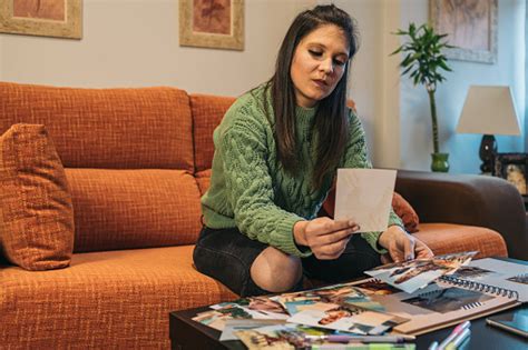 중년의 갈색 머리 여자는 소파에 앉아 여행 사진과 와시 테이프로 수제 크래프트 앨범을 만들기 위해 더미에서 사진을 찍고 있다 30 34세에 대한 스톡 사진 및 기타 이미지