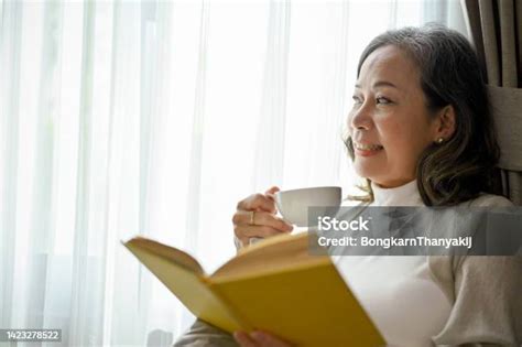 좋아하는 책을 읽으며 모닝 커피를 마시는 매력적인 아시아 중년 여성 노인에 대한 스톡 사진 및 기타 이미지 노인 여자 여자만 Istock