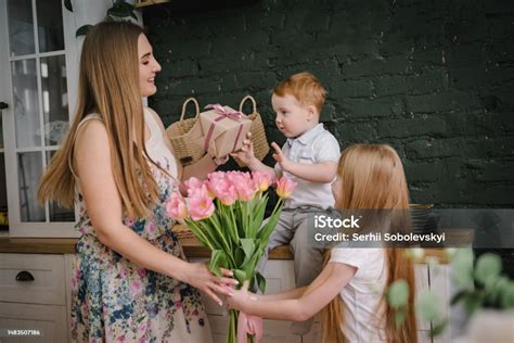 생일 축하해요 아이들과 함께 엄마는 놀랐다 아이들은 어머니를 축하하고 집에 있는 부엌에서 튤립 꽃다발을 선물합니다 어머니의 날 개념입니다 인사말 카드 여성의 날 뒷모습 2