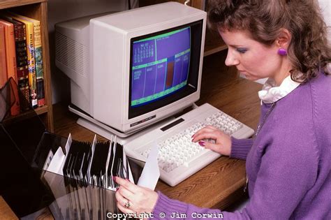 A Woman Sitting At A Desk Using A Computer With A Monitor And Keyboard In Front Of Her