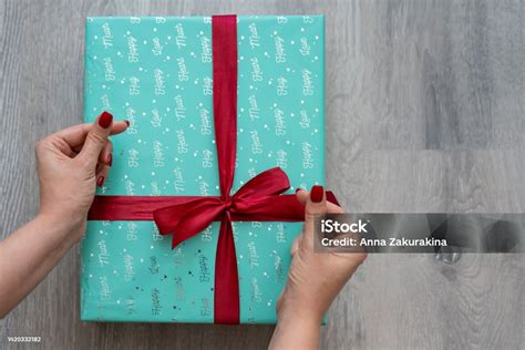 회색 나무 배경에 빨간 리본 활이있는 녹색 청록색 선물 상자를 들고있는 여자 손 개념 휴일 축하 생일 새해 크리스마스 발렌타인 데이 어머니의 날 추수 감사절 개념에 대한