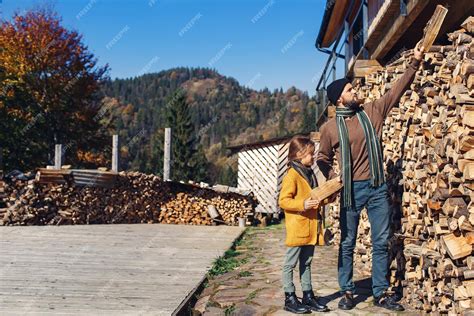 Premium Photo Daughter Helps Father To Stack Chopped Firewood Gives Him Pieces Of Wood