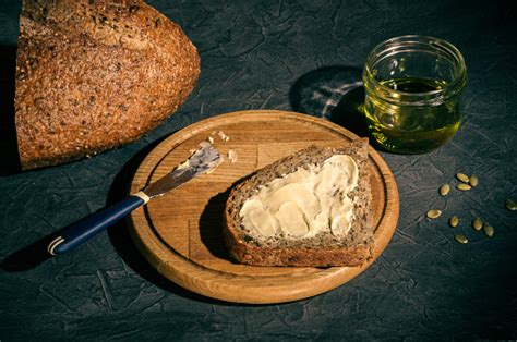 아마 양귀비 씨앗 참깨 기장 호박 해바라기 씨와 소박한 천연 효모가없는 빵 조각 버터와 함께 확산 나무 보드에 유리 항아리에 올리브 오일 검은 배경 하드 라이트 낮은 키에