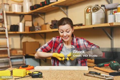 격자 무늬 셔츠 회색 티셔츠에에서 백인 젊은 여 자가 노란색 장갑 나무 테이블에서 목공 워크숍에서 일하고 다른 도구 망치 보드로 후 펜 치로 못 밖으로 데리고와 장소 Diy