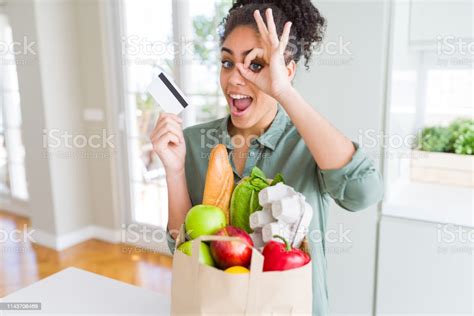 젊은 아프리카계 미국인 소녀 들고 행복 한 얼굴로 지불으로 식료품 및 신용 카드의 종이 봉지는 눈에 손으로 확인 표시를 하 고