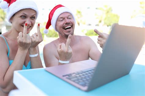 빨간 산타 클로스 모자를 쓴 즐거운 남자와 여자는 수영장에서 리조트에있는 노트북 모니터에서 사실의 제스처를 보여줍니다 전화에 대한 스톡 사진 및 기타 이미지 Istock