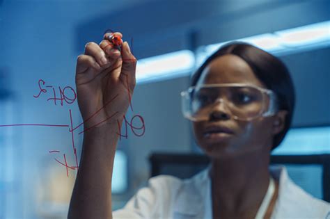 유리 판 뒤의 젊은 사려 깊은 아프리카 계 미국인 과학자 제약 분야의 과학 연구 중에 그 보드에 쓰여진 화학 공식을 살펴 봅니다