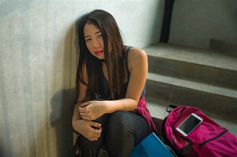 아시아 여자 대학생 괴롭힘의 극적인 초상화 젊은 우울하고 슬픈 일본 소녀는 괴롭힘과 괴롭힘이 절망적이고 배제된 것을 겪고 있는 캠퍼스 계단에 외로운 앉아 있습니다 계단에