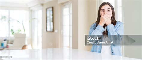 집에서 흰색 테이블에 앉아 아름다운 젊은 여성의 광각 사진은 실수로 손으로 입을 덮고 충격 비밀 개념입니다 가리기에 대한 스톡 사진 및 기타 이미지 Istock