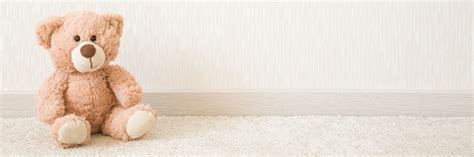 웃는 갈색 부드러운 테디 베어 밝은 회색 벽 배경에서 부드러운 흰색 홈 카펫에 앉아 와이드 배너 텍스트 인용문 또는 속담을 위한 빈 공간 근접 촬영 정면 View 가정