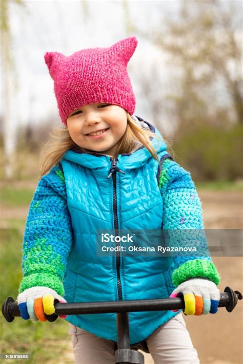 파란색 재킷과 분홍색 모자를 쓴 어린 쾌활한 소녀가 교외 야외에서 자전거에 앉아있는 카메라를 바라 봅니다 금발 머리에 대한 스톡 사진 및 기타 이미지 Istock