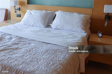 나무와 유리 헤드보드가 있는 더블 침대 흰색 베개 접힌 이불 침대 협탁에 있는 복고풍 알람 시계 벽걸이형 전기 램프 전경에 초점 알람시계에 대한 스톡 사진 및 기타 이미지