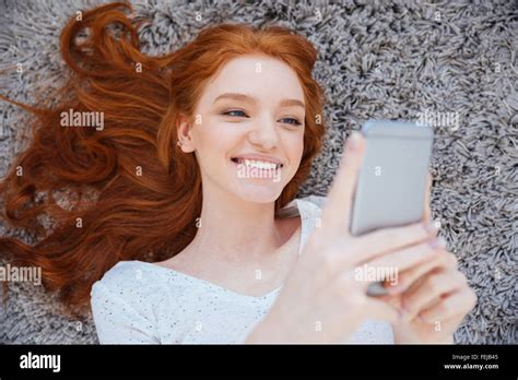 Smiling Redhead Woman Lying On The Carpet And Using Smartphone At Home Stock Photo Alamy