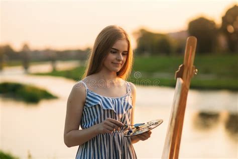 Красивая девушка рисует изображение в парке используя палитру с