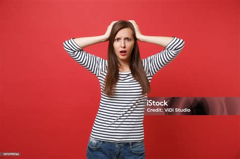 줄무늬 옷 서 고 밝은 빨간 벽 배경에 고립 된 머리에 손을 댔이 충격된 난처 한 젊은 여자의 초상화 사람들이 진심으 감정 라이프 스타일 개념 복사 공간을 비웃는 다 갈색