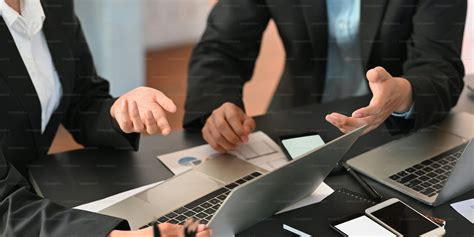 현대 사무실을 배경으로 검은 회의 테이블에 함께 앉아 컴퓨터 노트북과 그래픽 차트로 사업 계획에 대해 논의하는 비즈니스 임원의