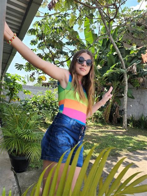 금속 난간 미소 짓는 여성 평화의 V사인 포즈 푸른 나무에 관한 무료 스톡 사진