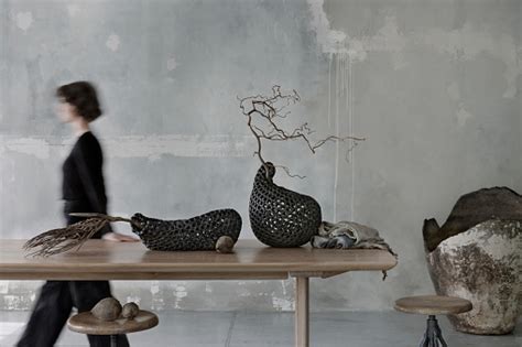 걷는 여성 나무 테이블 회색 콘크리트 벽 가지가 있는 세련된 꽃병 둥근 의자 및 개인 액세서리가 있는 Japandi 식당 인테리어의 원시 구성 가정 장식 템플렛 가구에 대한