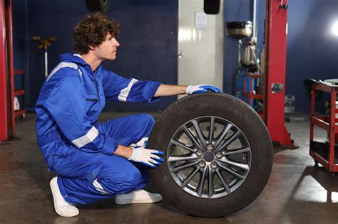 제복을 입은 남자 기술자 자동차 정비공이 수리 차고에서 교체하거나 교체하기 위해 타이어를 들고 있는 모습 자동차 센터 수리
