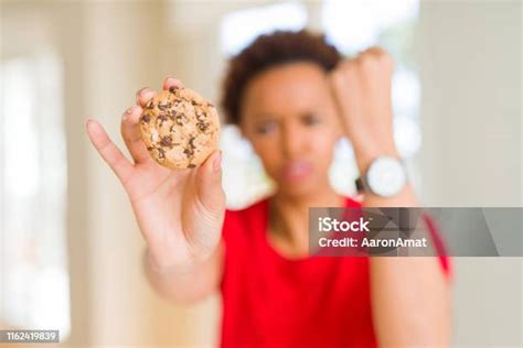 초콜릿 칩 쿠키를 먹는 젊은 아프리카 계 미국인 여성은 짜증과 분노와 함께 고함 미친 소리와 함께 고함 제기 손으로 소리 분노 개념 불쾌한에 대한 스톡 사진 및 기타 이미지