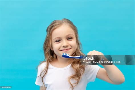 흰색 티셔츠를 입은 귀여운 어린 소녀는 파란색 배경에 칫솔로 이빨을 닦고 위생과 치과의 개념 텍스트 공간 이빨에 대한 스톡 사진 및 기타 이미지 Istock
