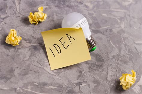 1 현대 플라스틱 Led 전구 그리고 비문 아이디어와 두 개의 노란 곡선된 종이 스티커 근처 오래 된 착용된 회색 콘크리트 바닥에 구겨진된 종이 공 3 비즈니스 개념 0명에