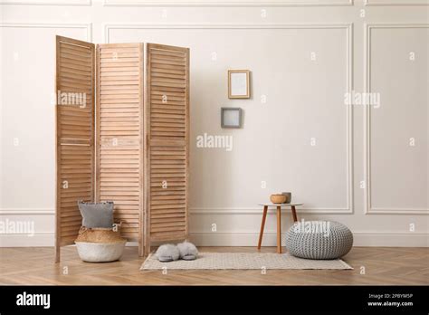 Folding Screen Small Table And Knitted Pouf Near White Wall In Room Interior Design Stock