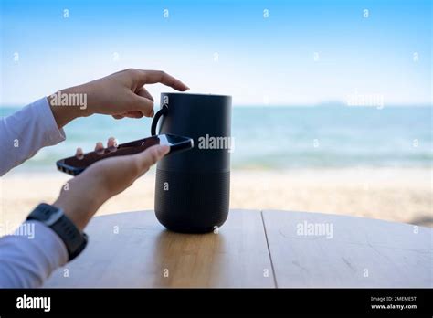 Hands Connecting Cell Phone With Bluetooth Speaker With Beach