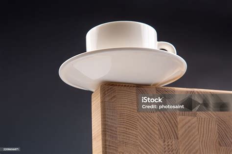 화이트 세라믹 컵은 어두운 배경과 대조를 이루며 나무 도마의 가장자리에서 위태롭게 균형을 이루며 따뜻한 나뭇결 질감의 눈에 띄고 미니멀한 구성을 만듭니다 0명에 대한 스톡