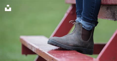 파란색 데님 청바지와 검은색 가죽 부츠를 신은 사람이 빨간 나무 벤치에 앉아 있다 사진 Unsplash의 무료 무딘 돌 이미지