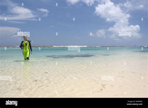 Woman In A Wetsuit With Snorkeling Equipment Walking Out Of The Water At A Beach In Cayman Brac