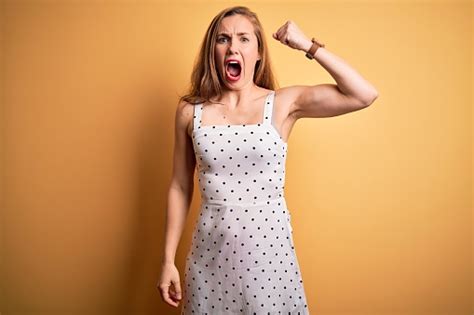 젊은 아름 다운 금발 여자 휴가 노란색 배경 화가 와 화가 주먹 을 제기 하는 동안 분노와 함께 외치는 동안 여름 드레스를 입고