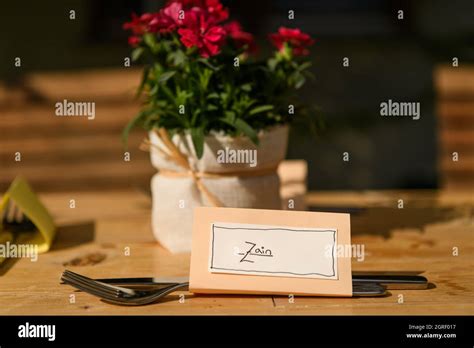 Hand Written Table Name Card And Cutlery On A Wooden Table Flowers In The Background Wedding
