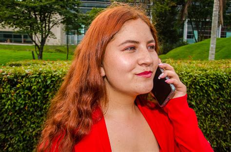 빨간 머리와 파란 눈을 가진 아름 다운 여자가 배경에 현대적인 건물과 함께 공공 공원에서 야외에서 스마트 폰을 사용 25 29